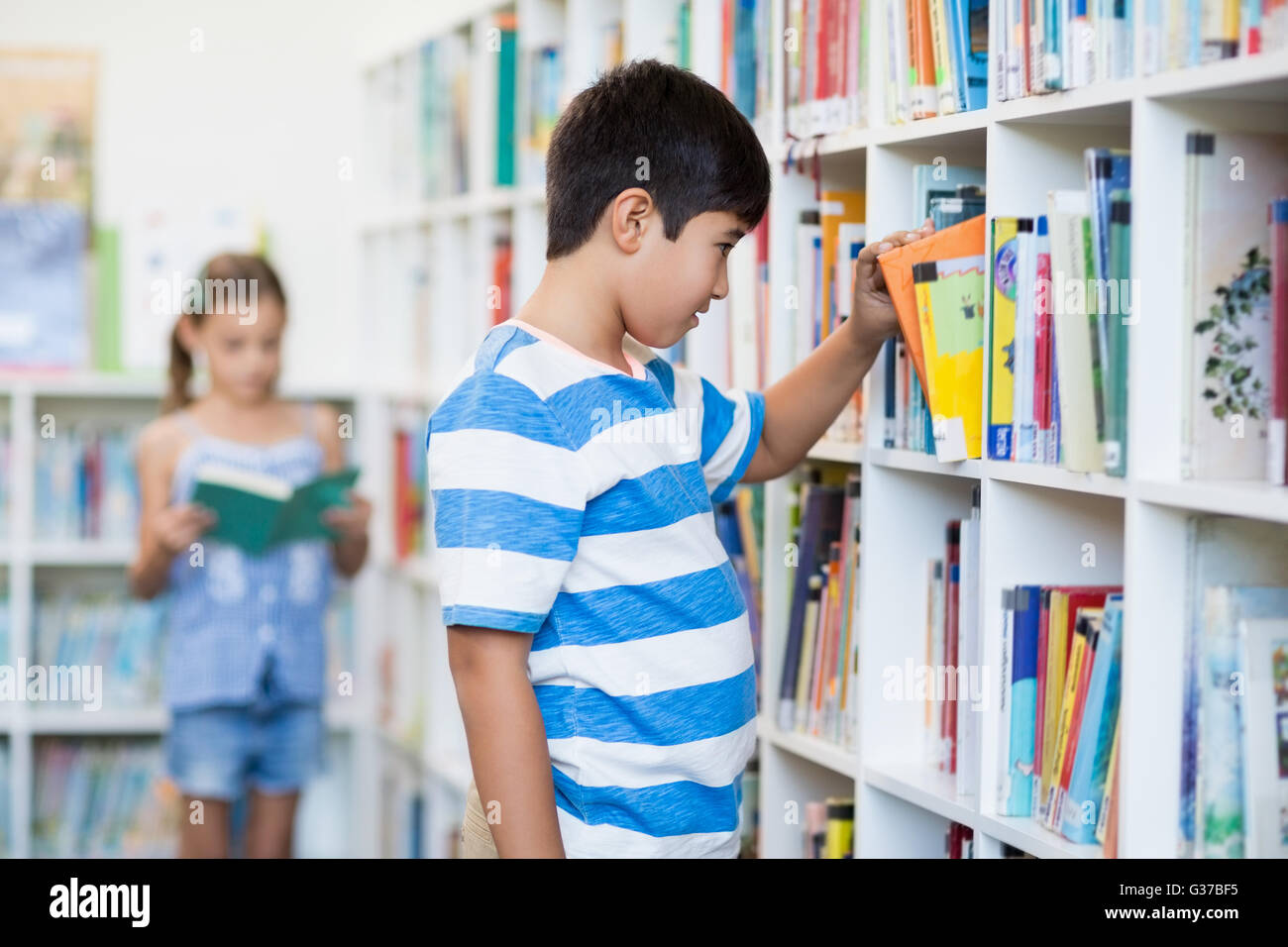 Boy taking a book from bookshelf in library Stock Photo - Alamy