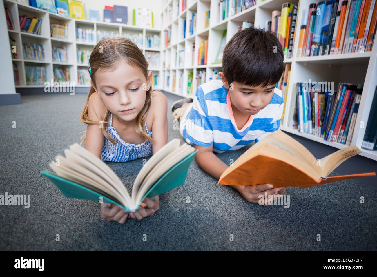 School kids lying on floor and reading a book in library Stock Photo ...