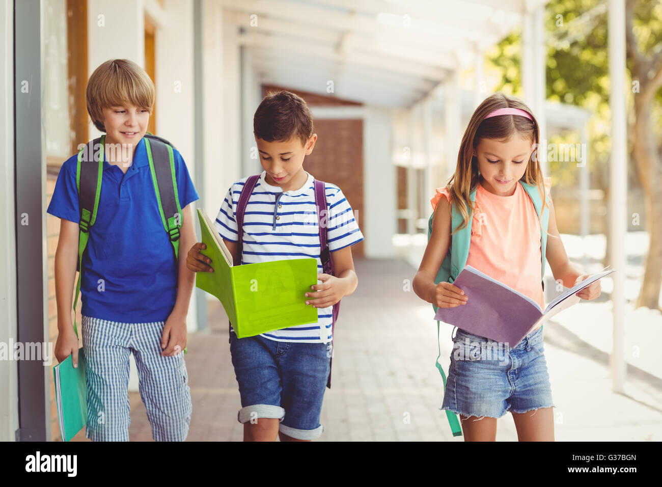 School kids reading books while walking in corridor Stock Photo - Alamy
