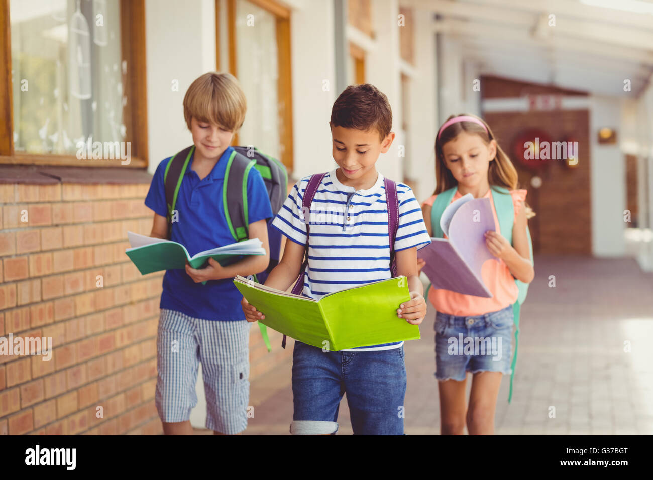 School kids reading books while walking in corridor Stock Photo - Alamy