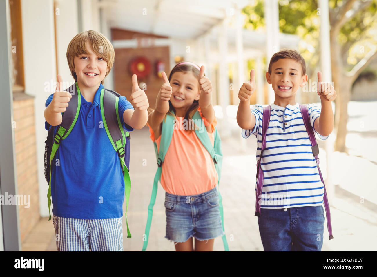 Smiling school kids showing thumbs up in school corridor Stock Photo ...