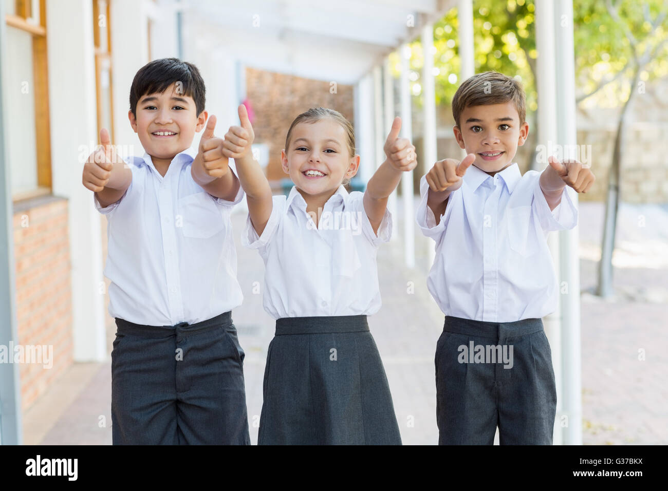 Smiling school kids showing thumbs up in corridor Stock Photo - Alamy