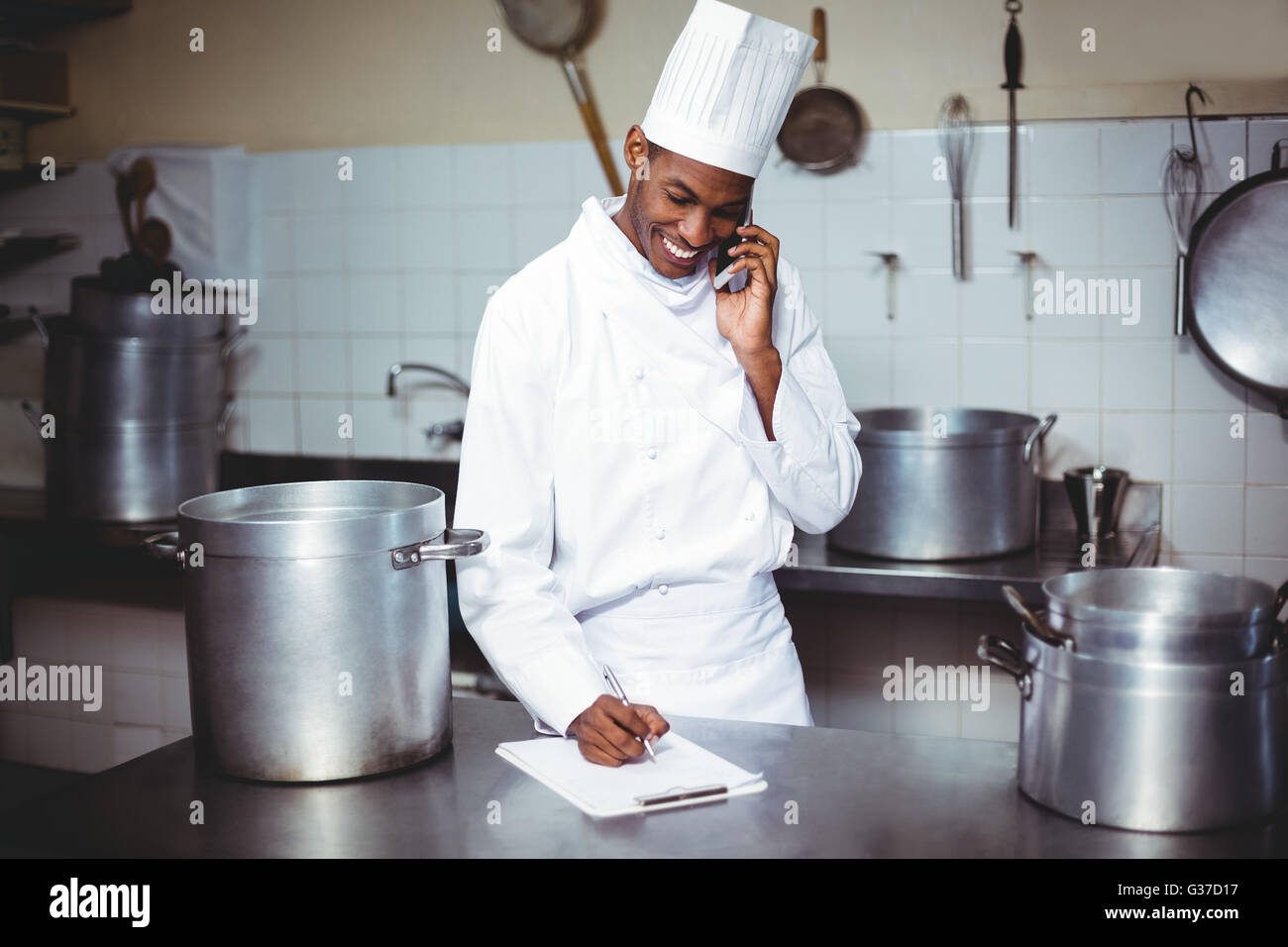 Chef writing on clipboard while talking on phone Stock Photo - Alamy