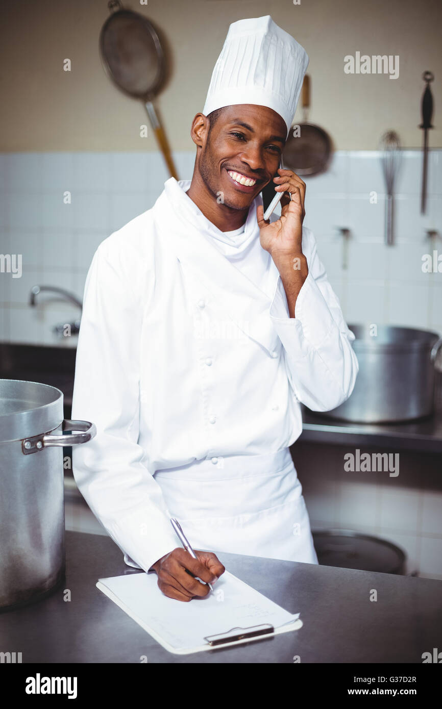 Chef writing on clipboard while talking on phone Stock Photo - Alamy