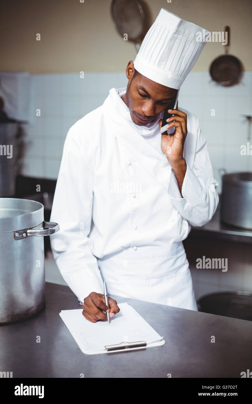 Chef writing on clipboard while talking on phone Stock Photo - Alamy