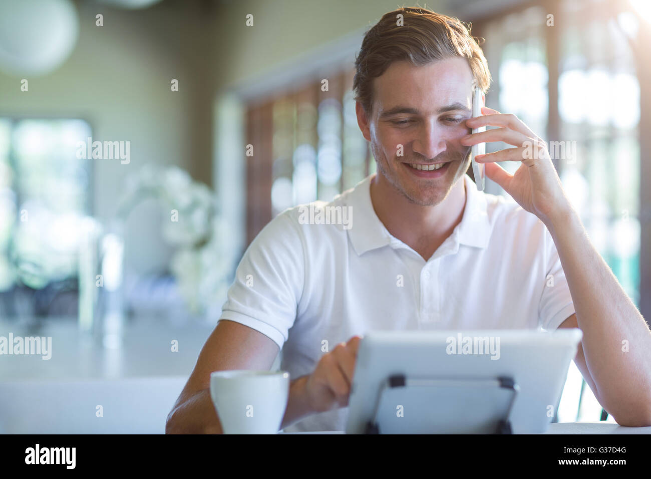 Smiling man talking on mobile phone while using digital tablet Stock ...
