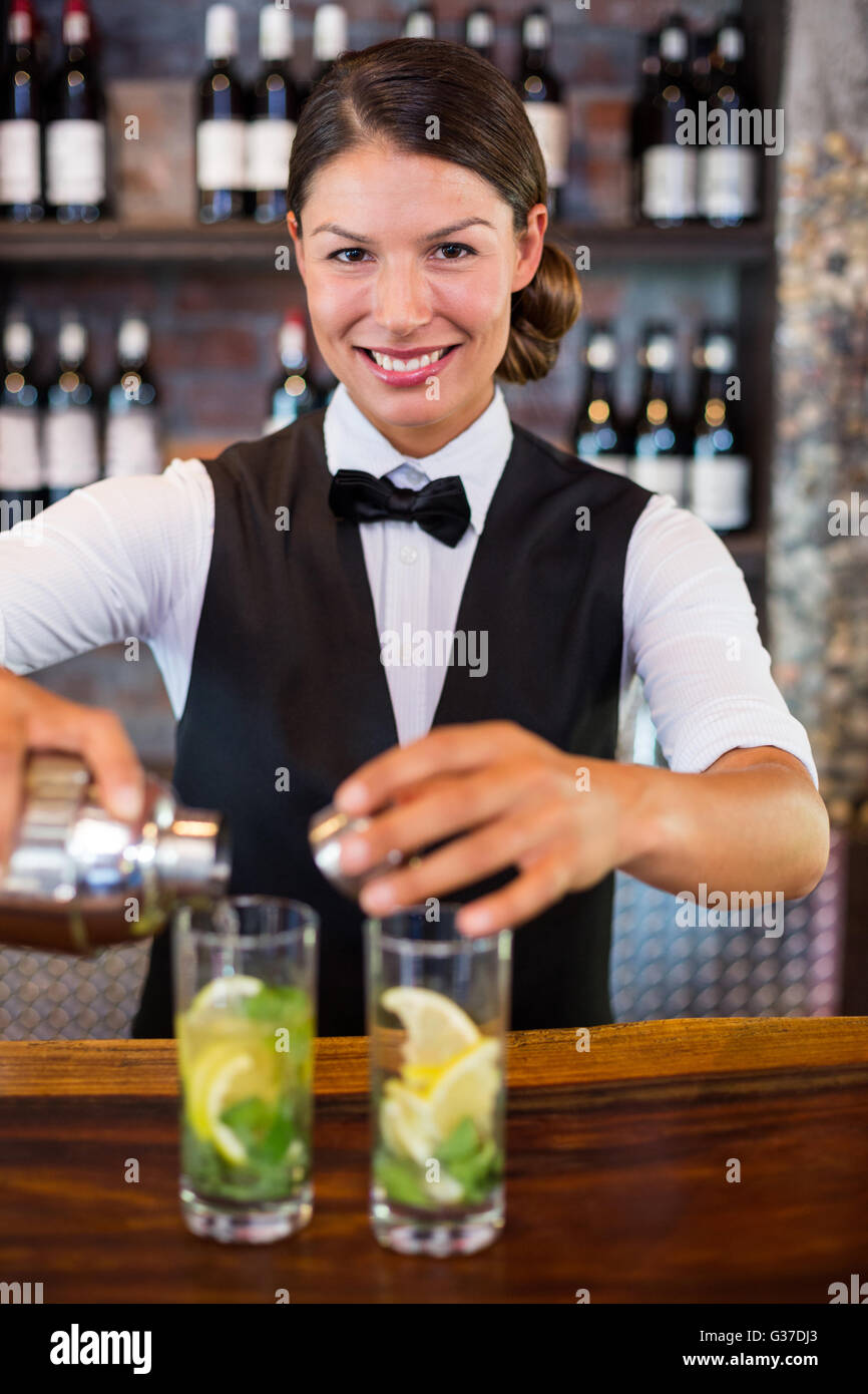 Portrait of bartender pouring a drink from a shaker to a glass on bar ...
