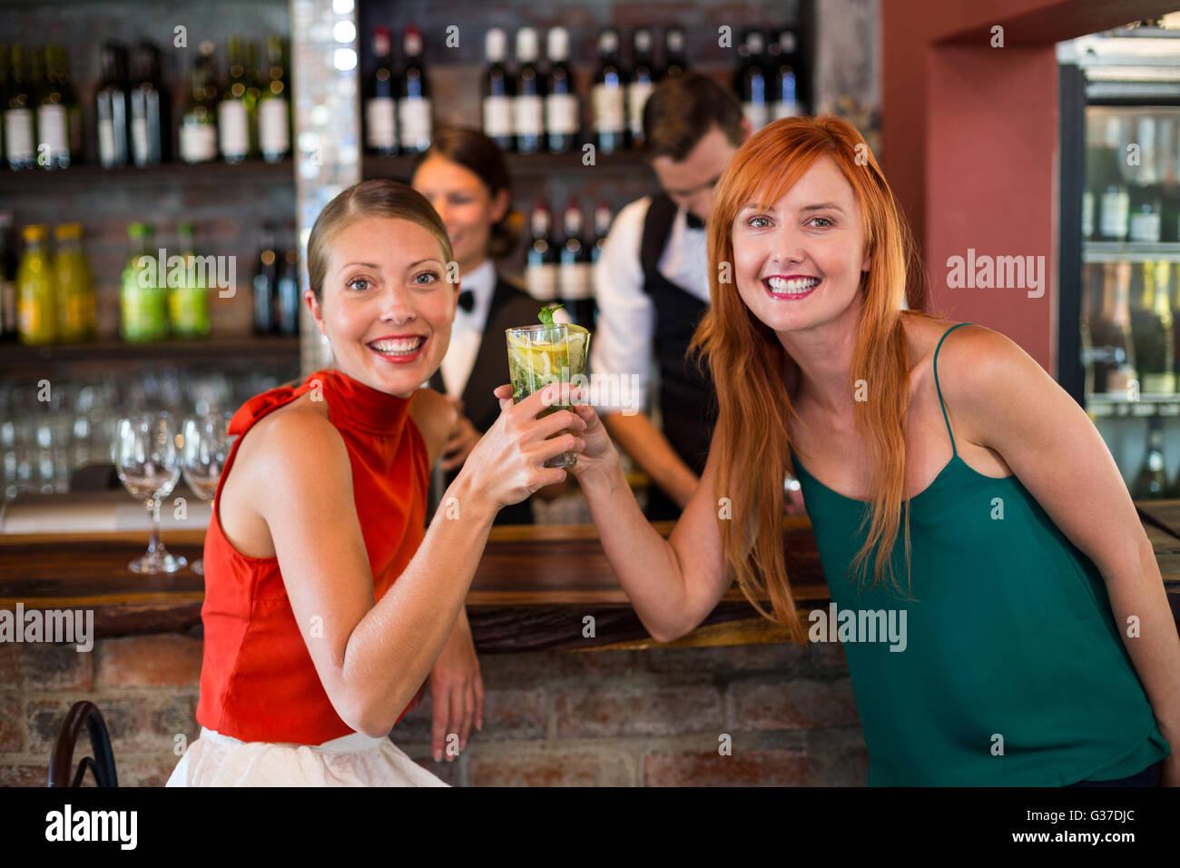 Portrait of happy friends holding a glass of gin in front of bar ...