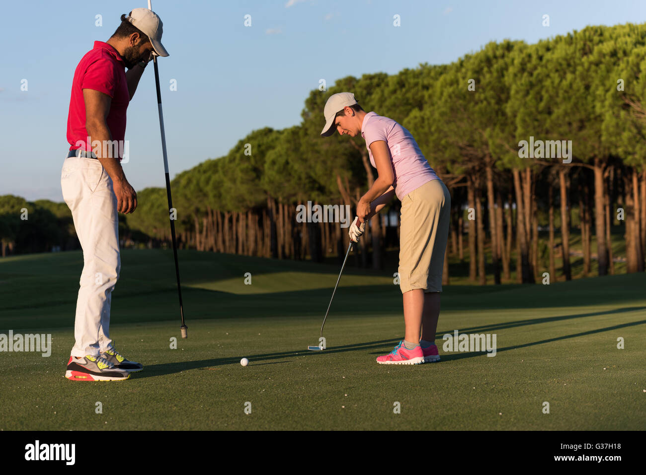 male golf instructor teaching female golf player, personal trainer ...