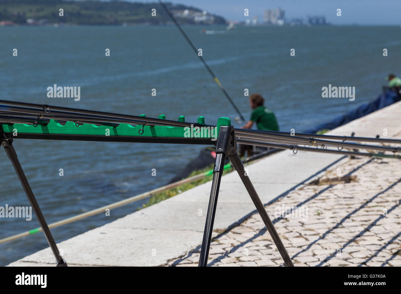 fishing stand with angling rods on promenade of river with fisher on ...