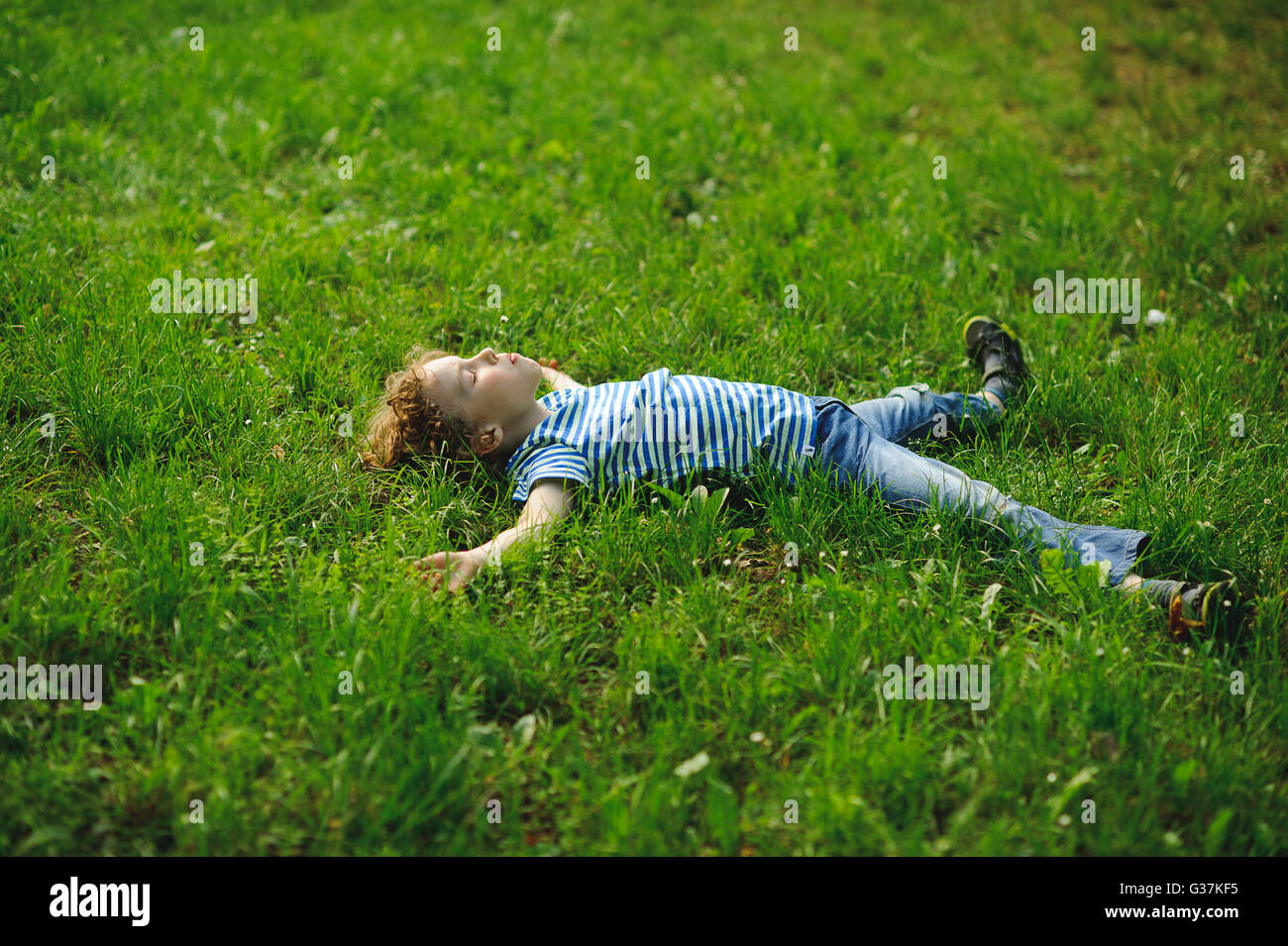 The boy lies in a dense green grass on a lawn. He lies on a back ...