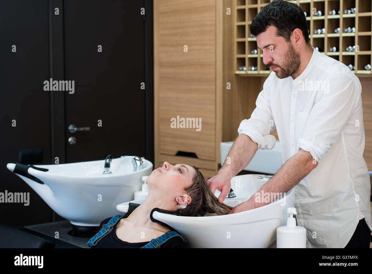Handsome hairdresser washing female hair with concentration. He is ...