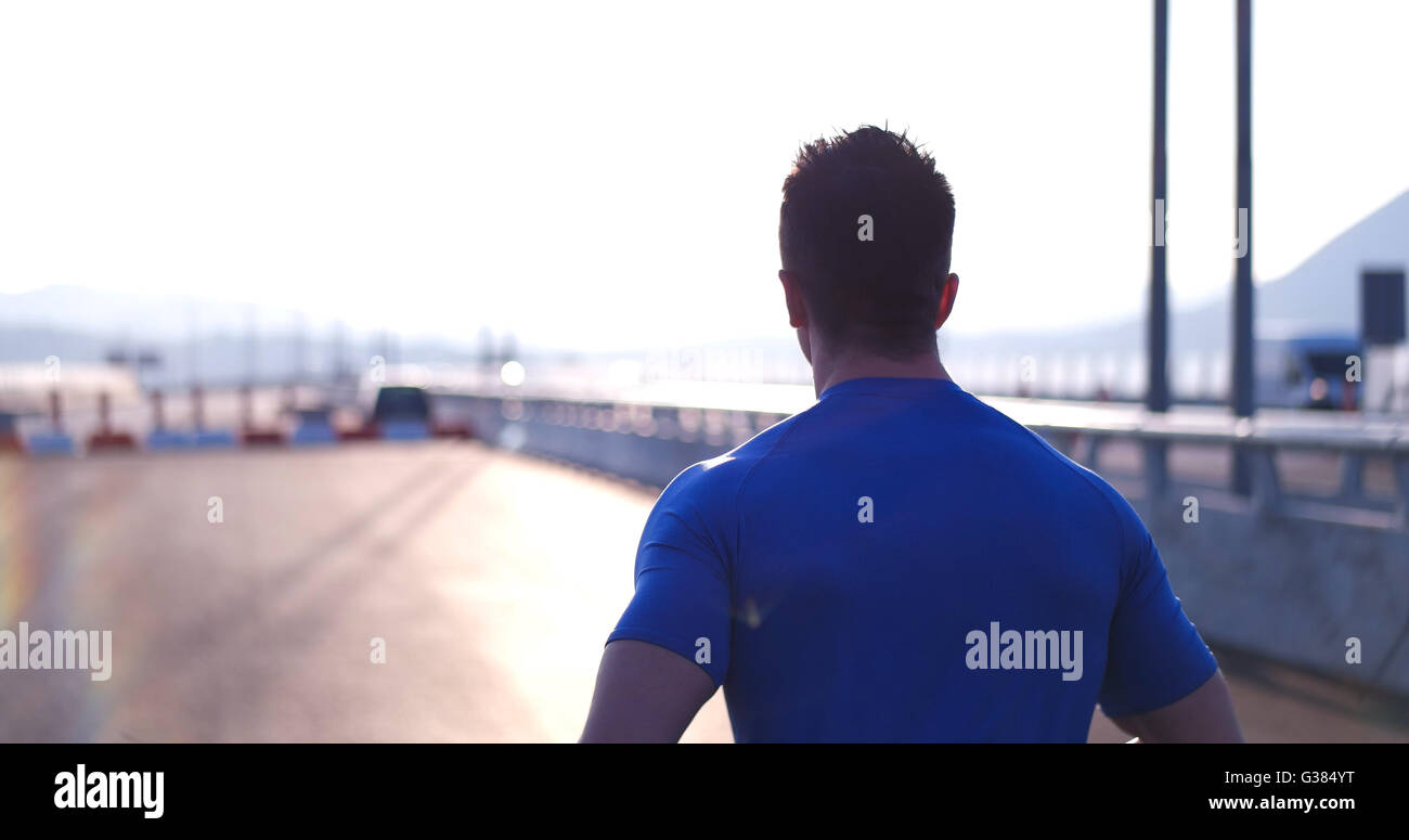 Attractive fit man running fast along big modern bridge at sunset light ...