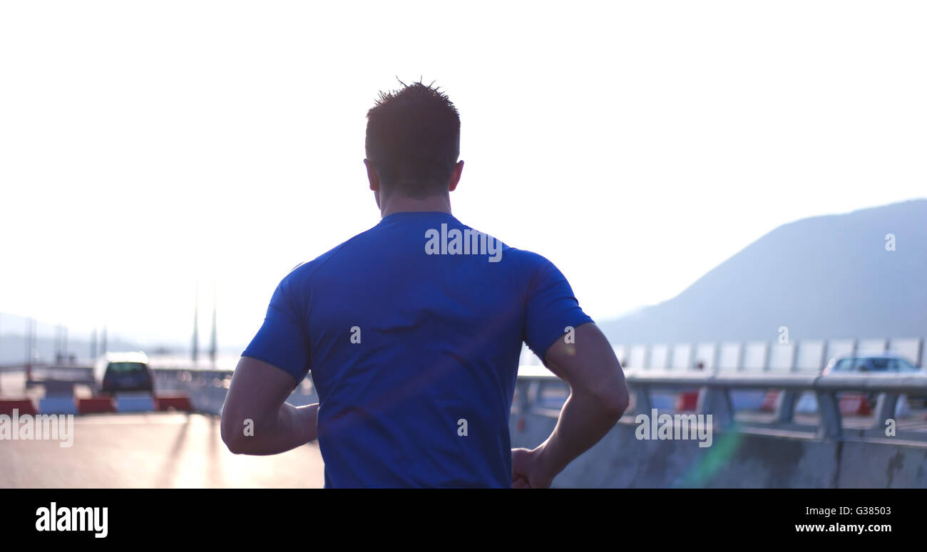 Attractive fit man running fast along big modern bridge at sunset light ...