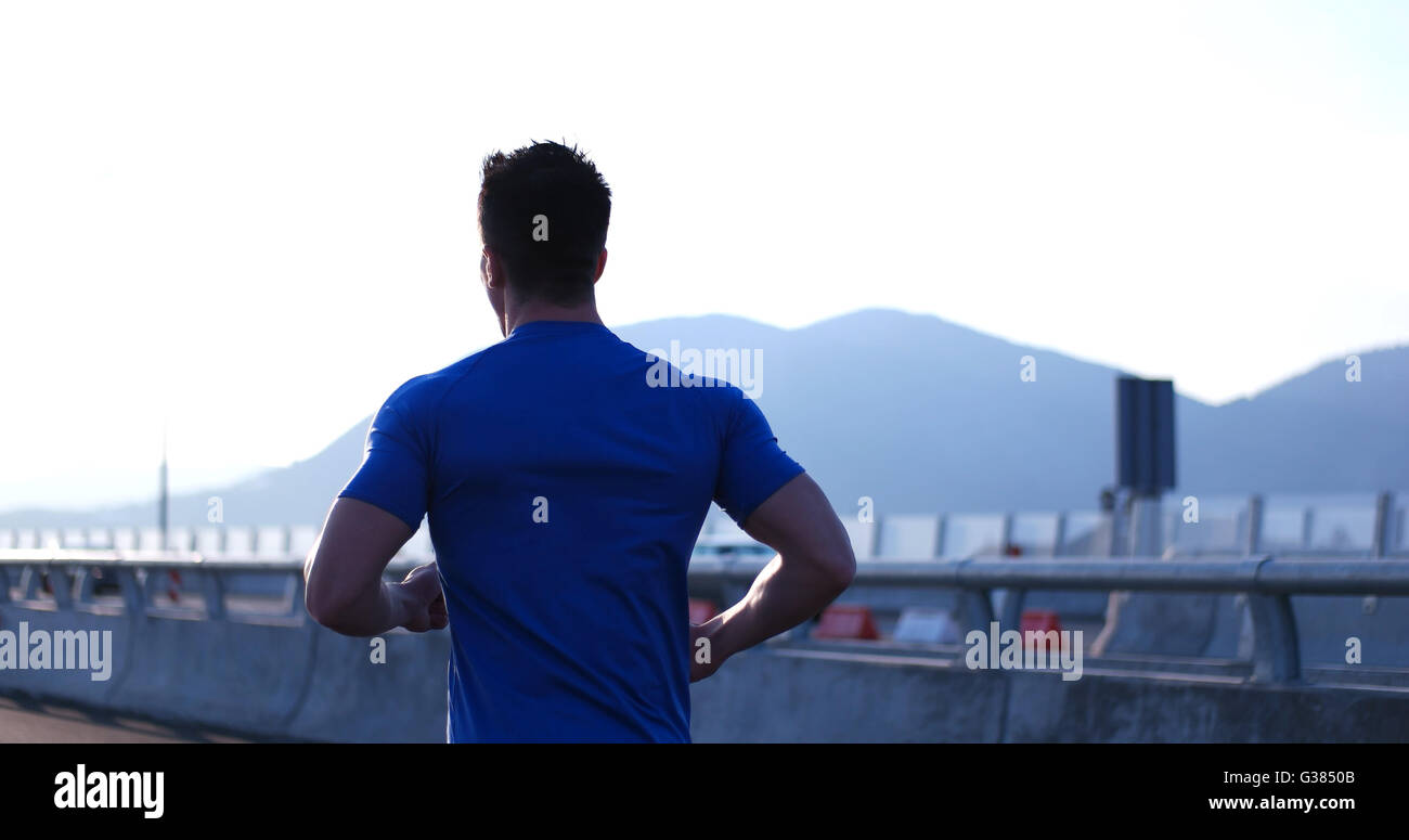 Attractive fit man running fast along big modern bridge at sunset light ...