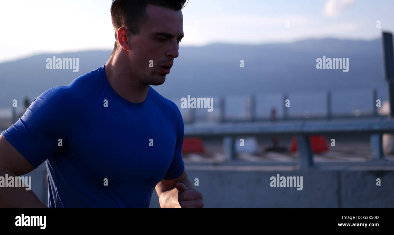 Attractive fit man running fast along big modern bridge at sunset light ...