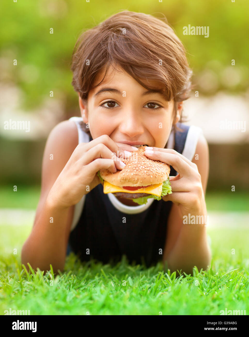Portrait of a hungry teen boy lying down on fresh green grass and ...