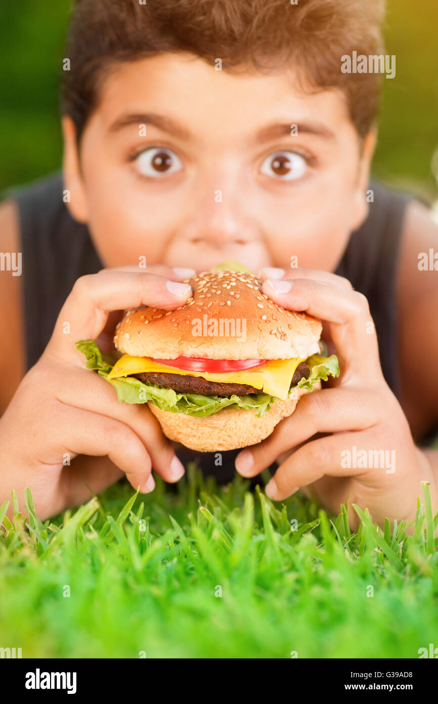 Portrait of a hungry teen boy lying down on fresh green grass and with ...