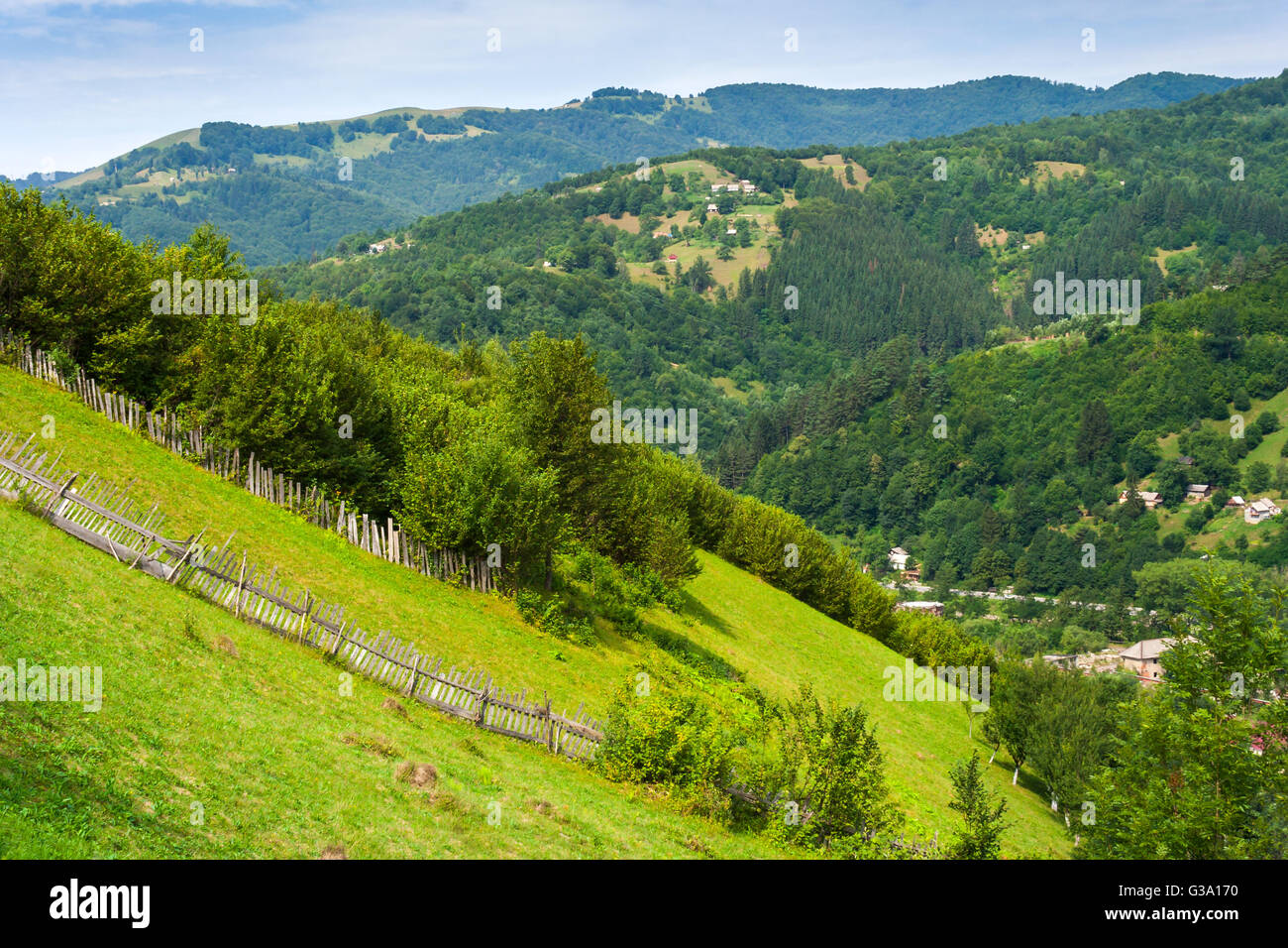 wooden stick fence in village in mountains with blue sky, green grass ...