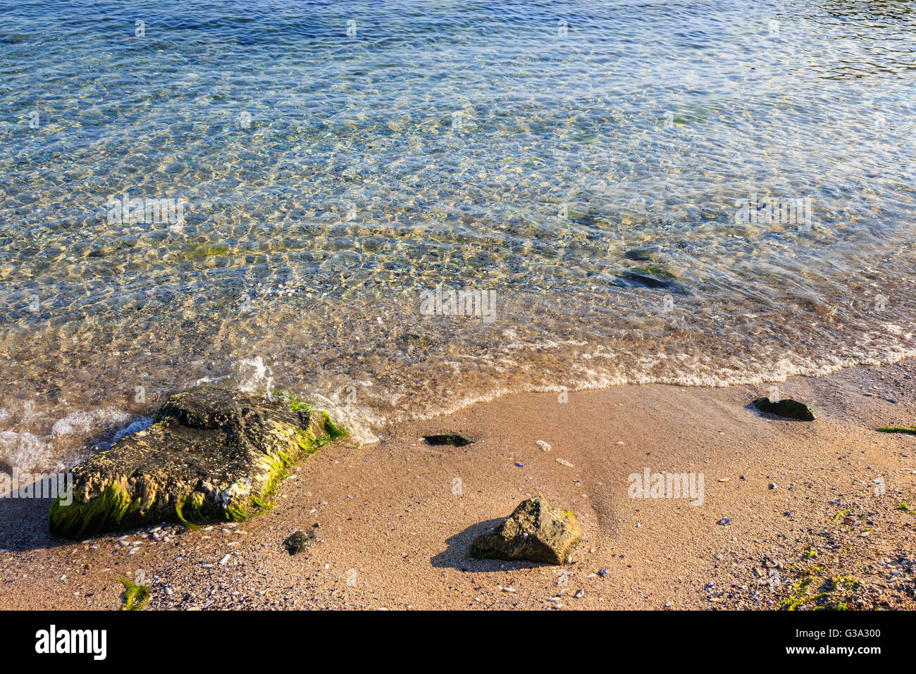 clean and clear sea waves wash sandy beach with few rocks Stock Photo ...