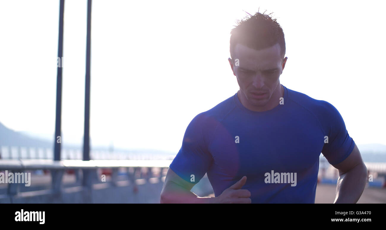 Attractive fit man running fast along big modern bridge at sunset light ...