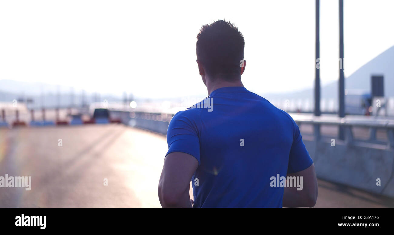 Attractive fit man running fast along big modern bridge at sunset light ...