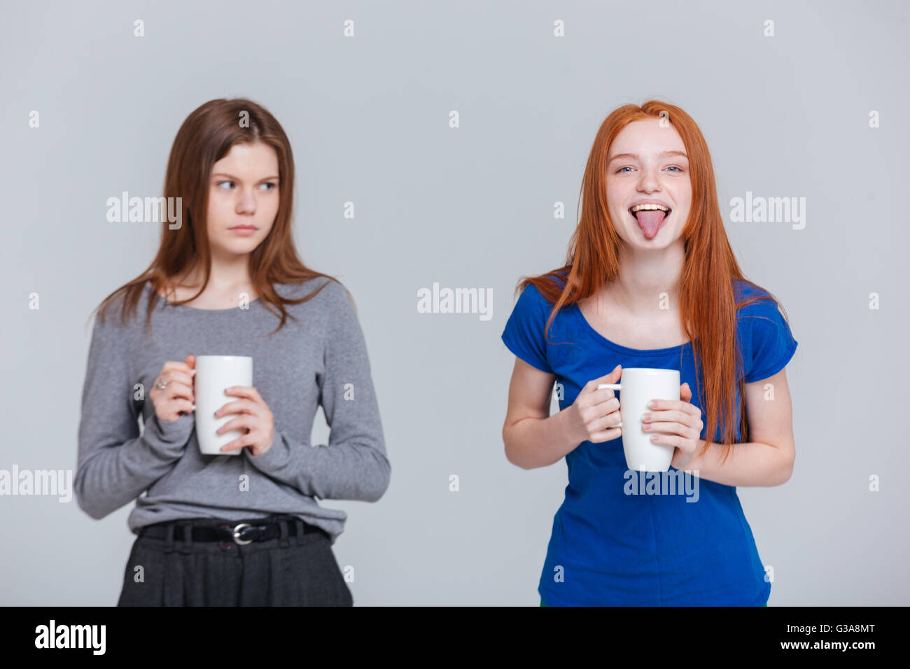 Two happy joking and sad frowning young women drinking tea from mugs ...