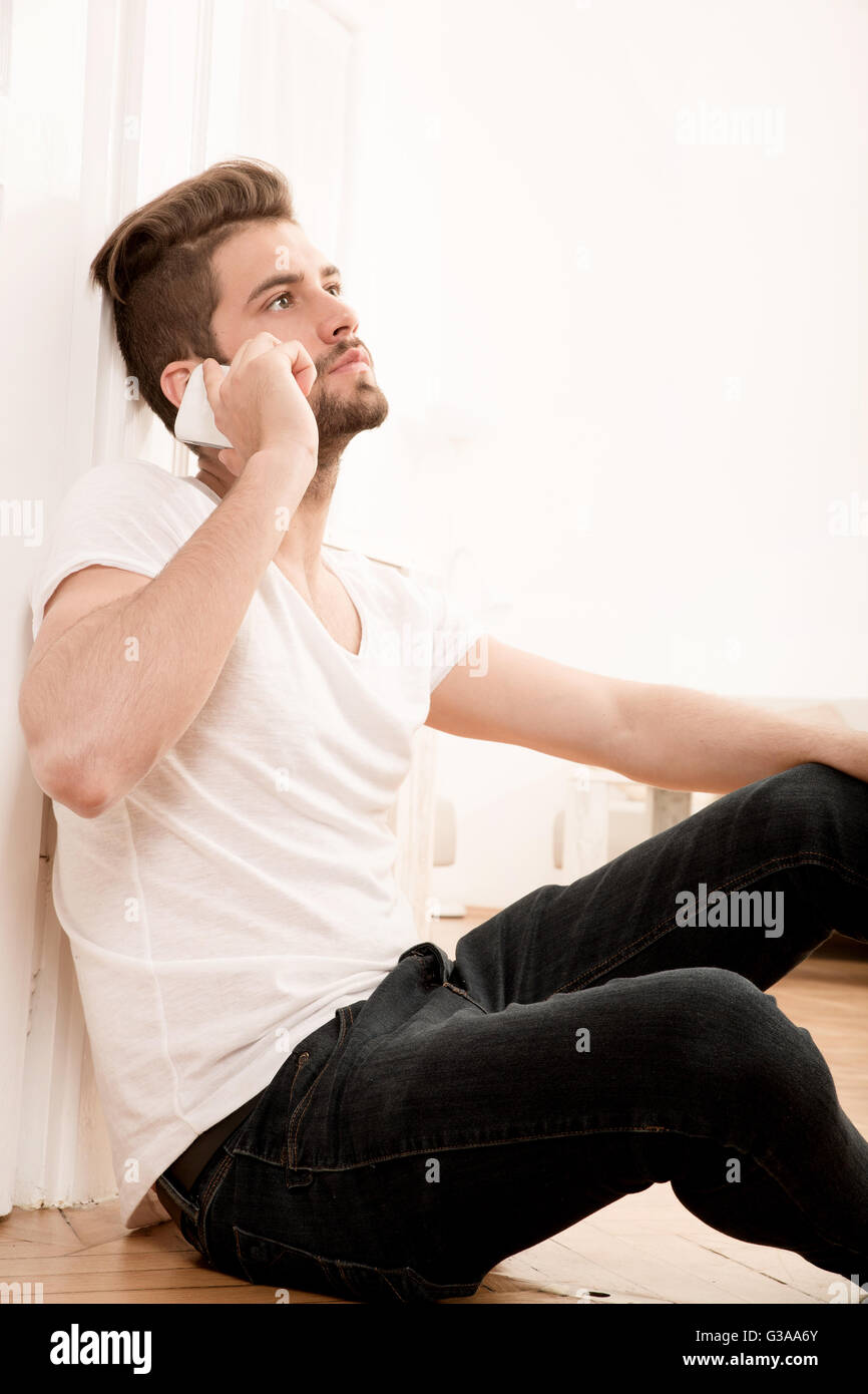 Portrait of an attractive man sitting on the floor using mobile phone ...