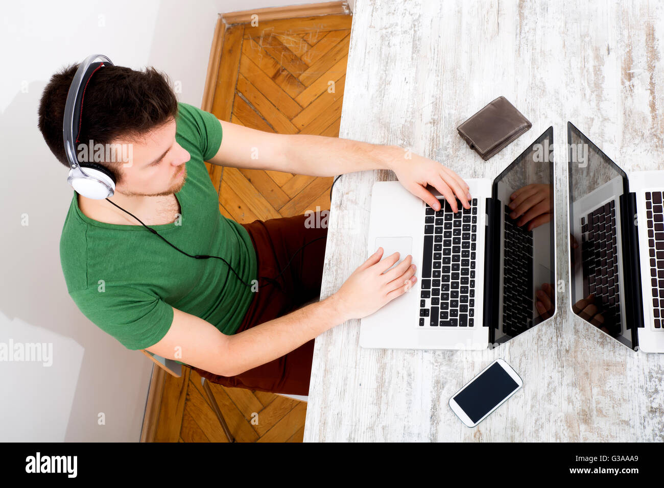 Young man typing on his laptop while listening to audio with headphones ...