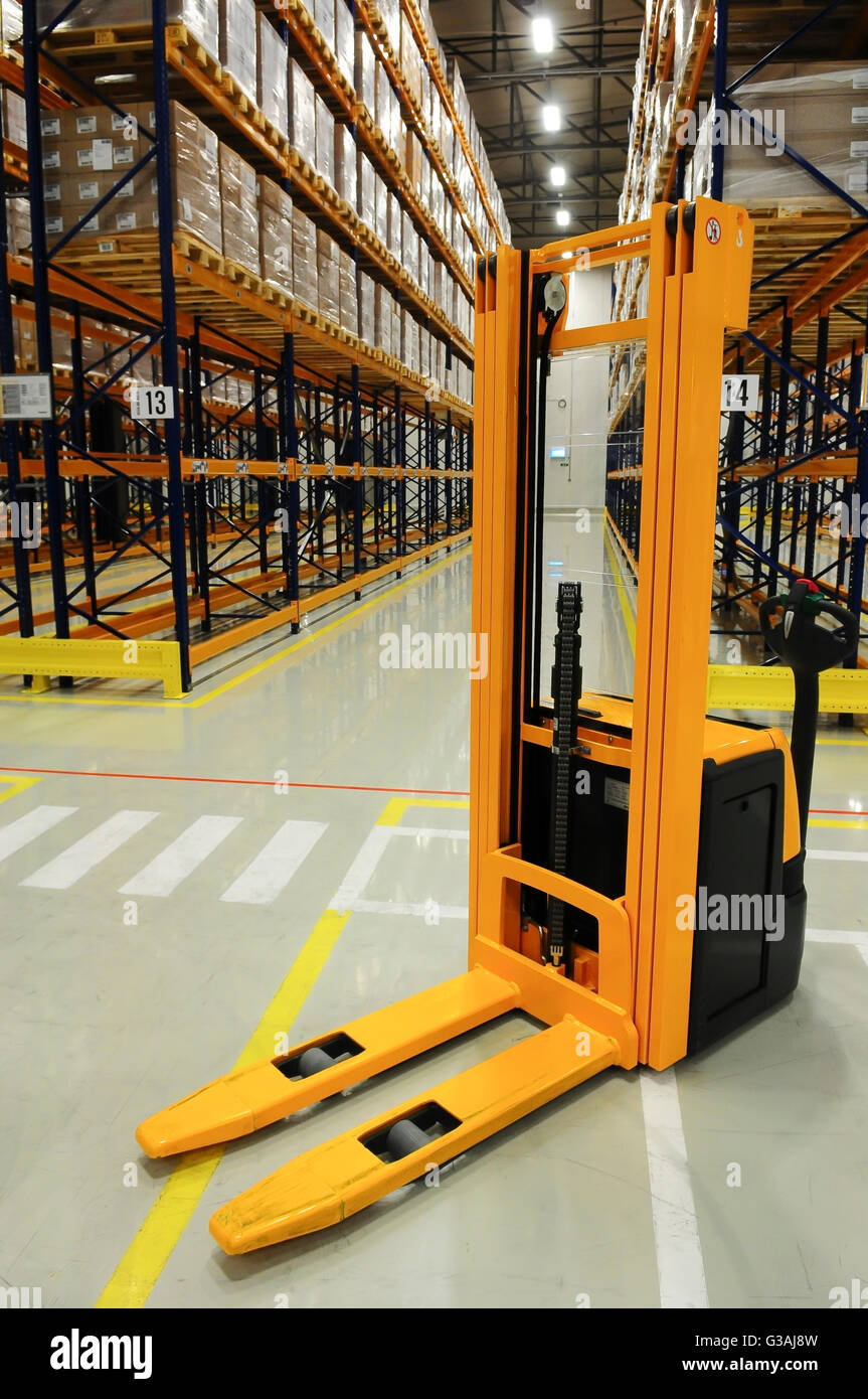 Yellow forklift in front, in back view through the racks of a large ...