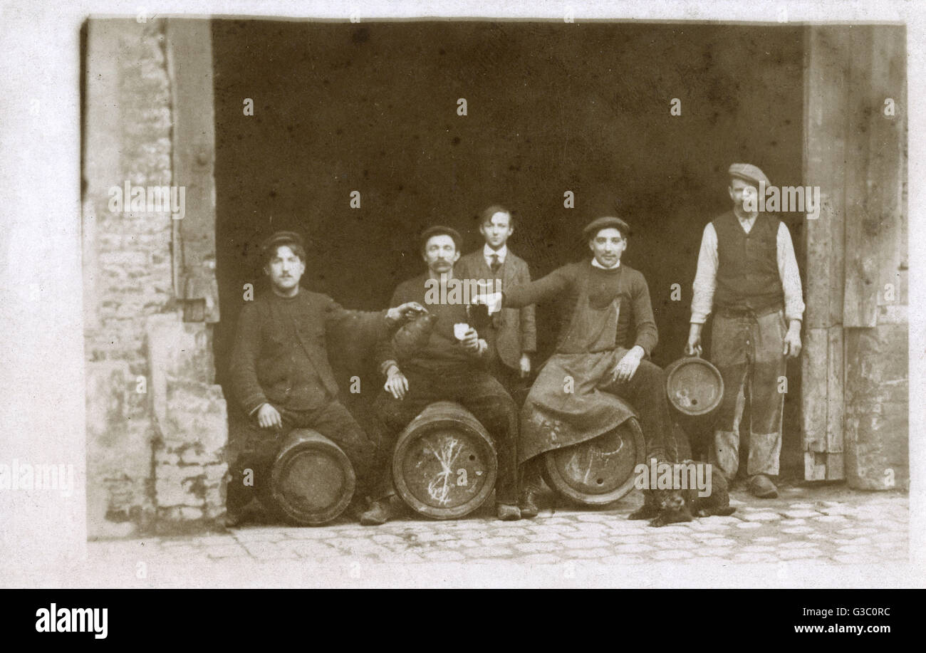 Group of working men sitting on barrels, with a dog, France. Date ...