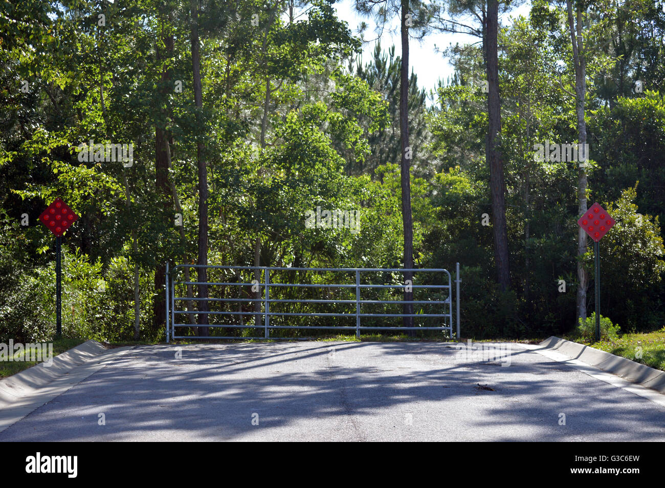 A paved, asphalt road leading to a metal gate with reflective signs on ...