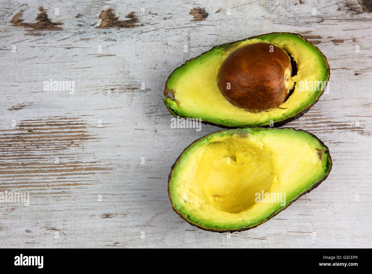 A fresh avocado cut into two halves with visible large pits on a wooden ...