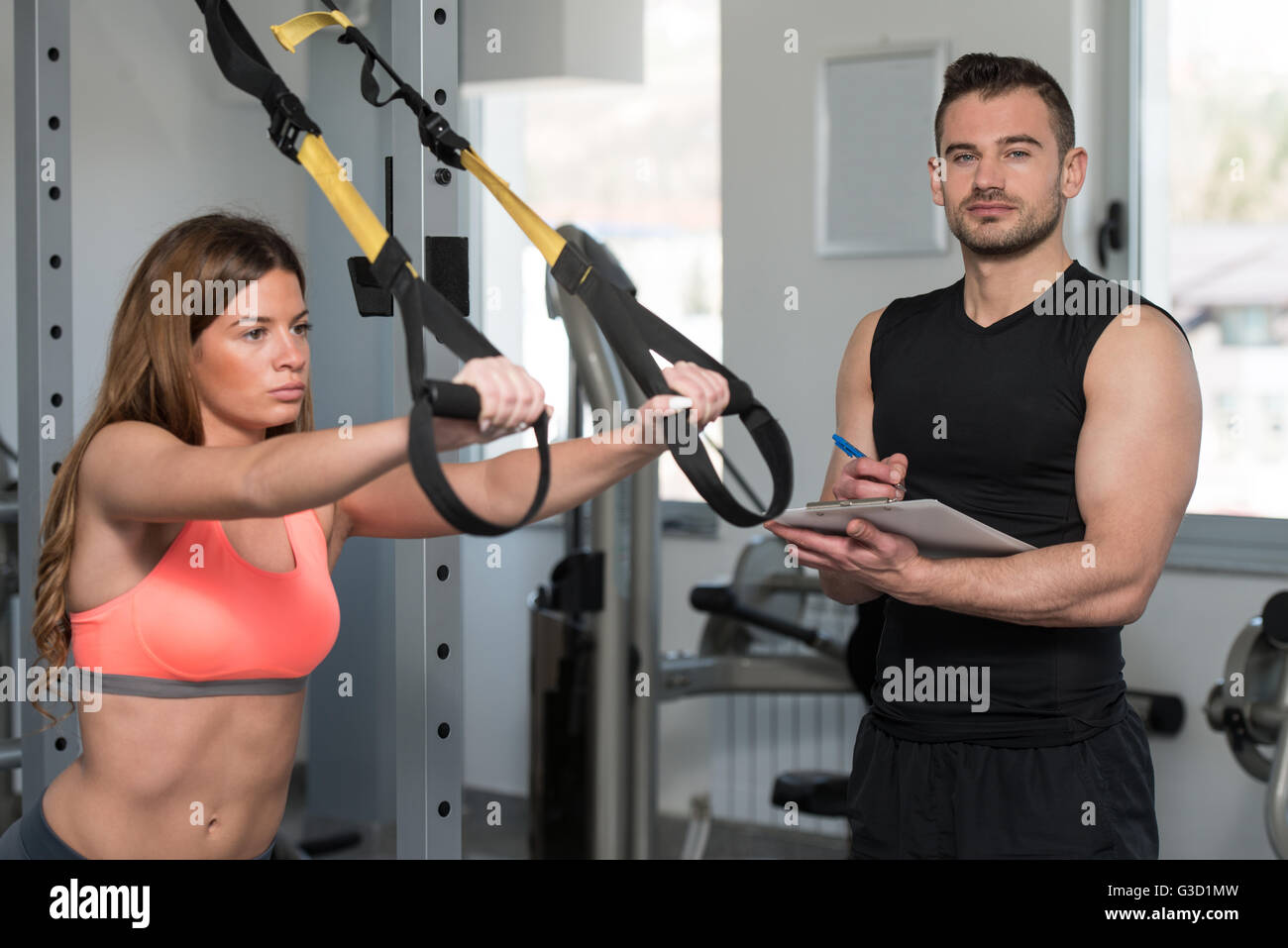 Personal Trainer Working With A Young Woman At The Gym Writing Notes On ...