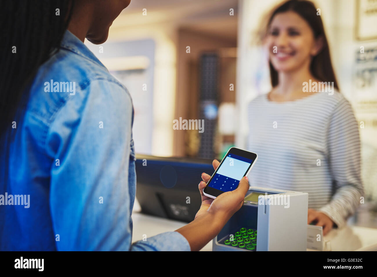 Customer paying with phone and pin pad in front of smiling cashier ...