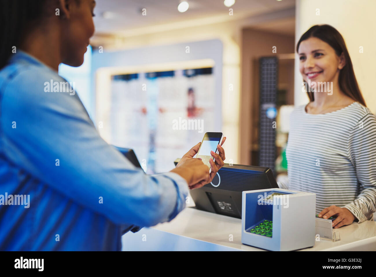 Customer paying for order with phone and pin pad in front of cheerful ...