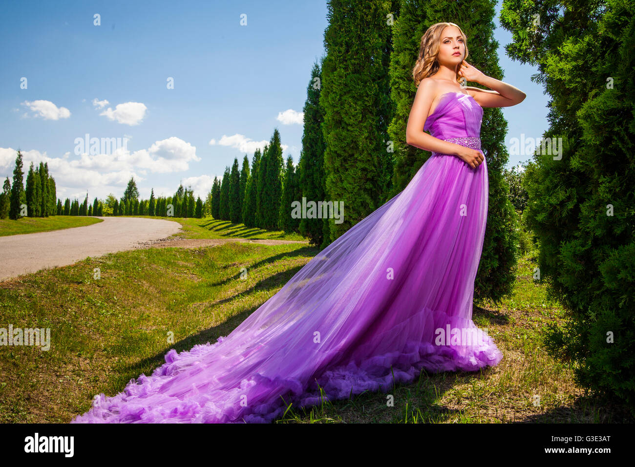 Elegant woman in violet long dress against of green alley Stock Photo ...