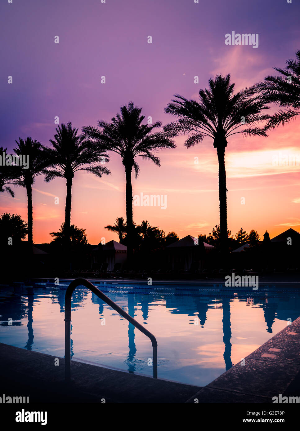 Sunset over pool with palm trees in silhouette against serene beautiful ...