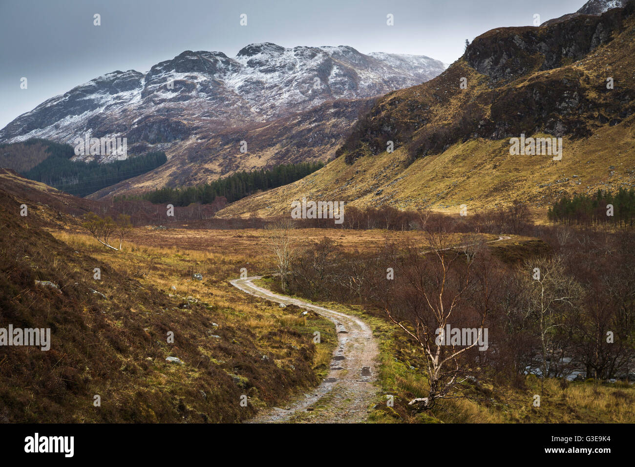 A winding single track through a Highland glen, snow covering the ...