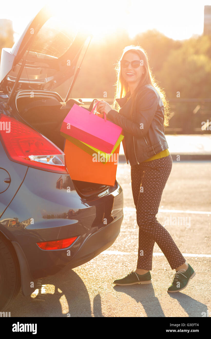 Smiling Caucasian woman putting her shopping bags into the car trunk ...