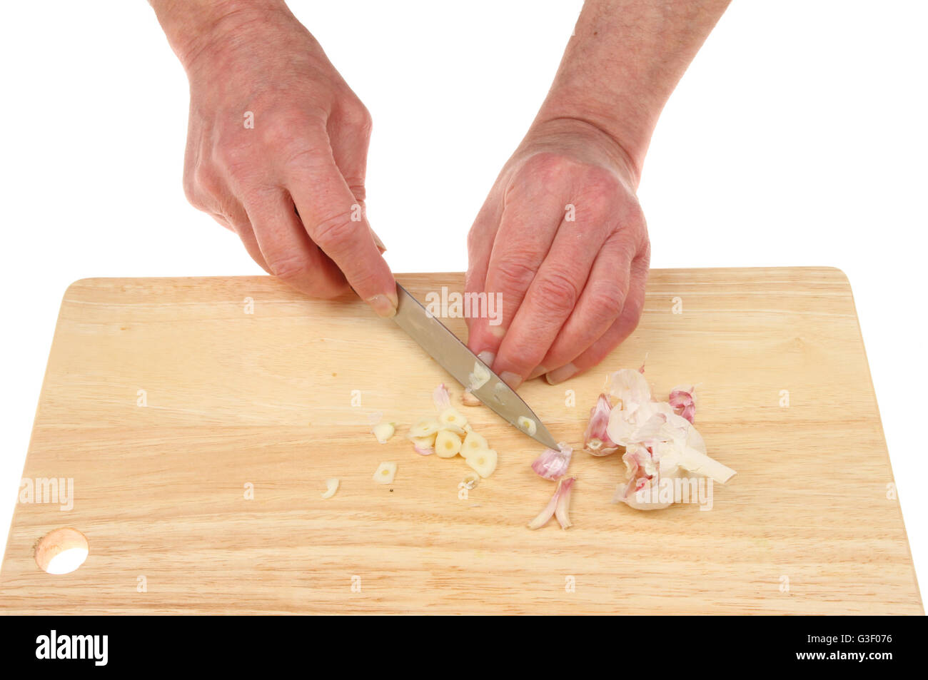 Hands chopping garlic on a wooden chopping board against a white ...
