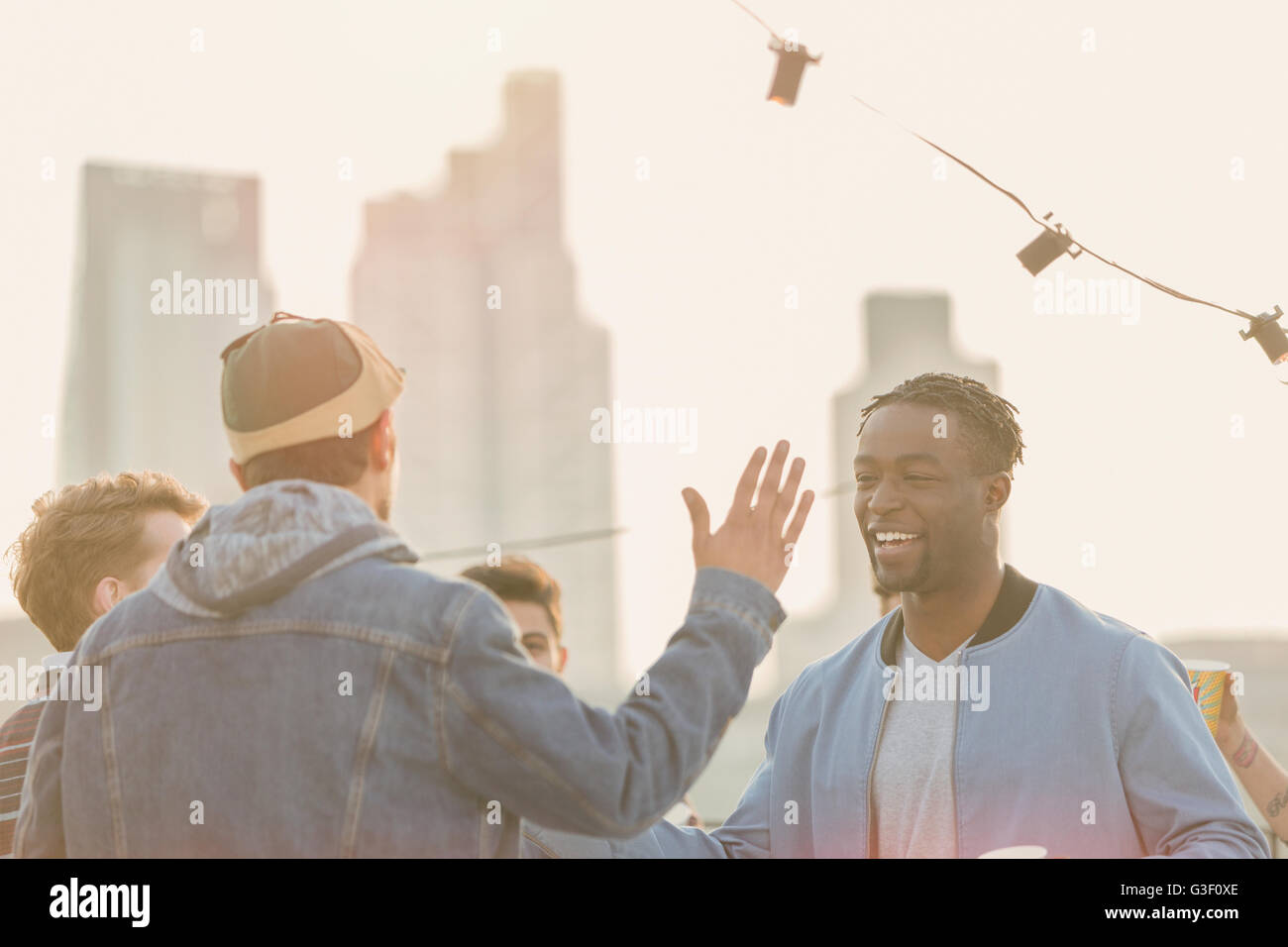 Young men high fiving at rooftop party Stock Photo - Alamy