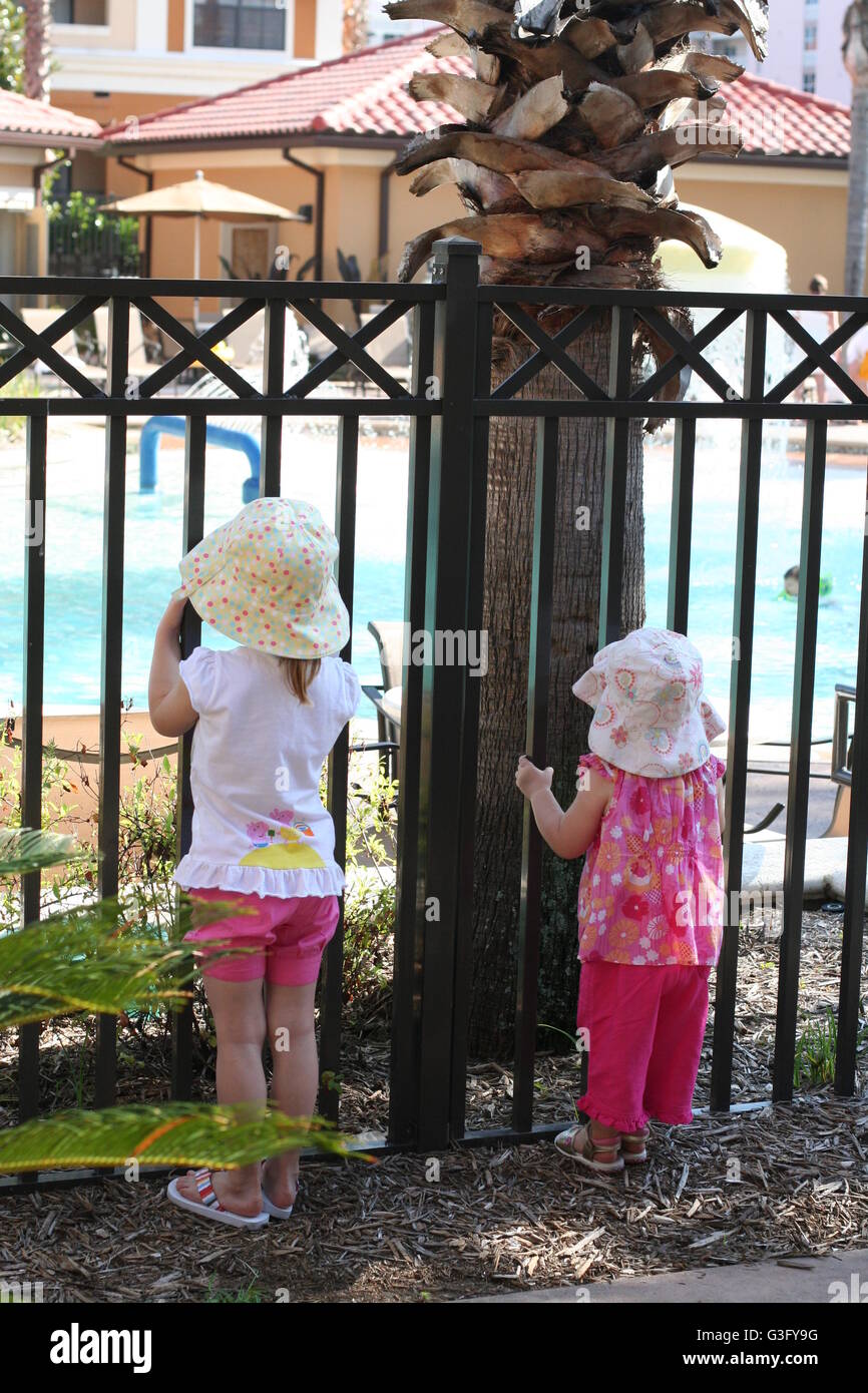 Little girls children standing looking in through a railings wrought ...