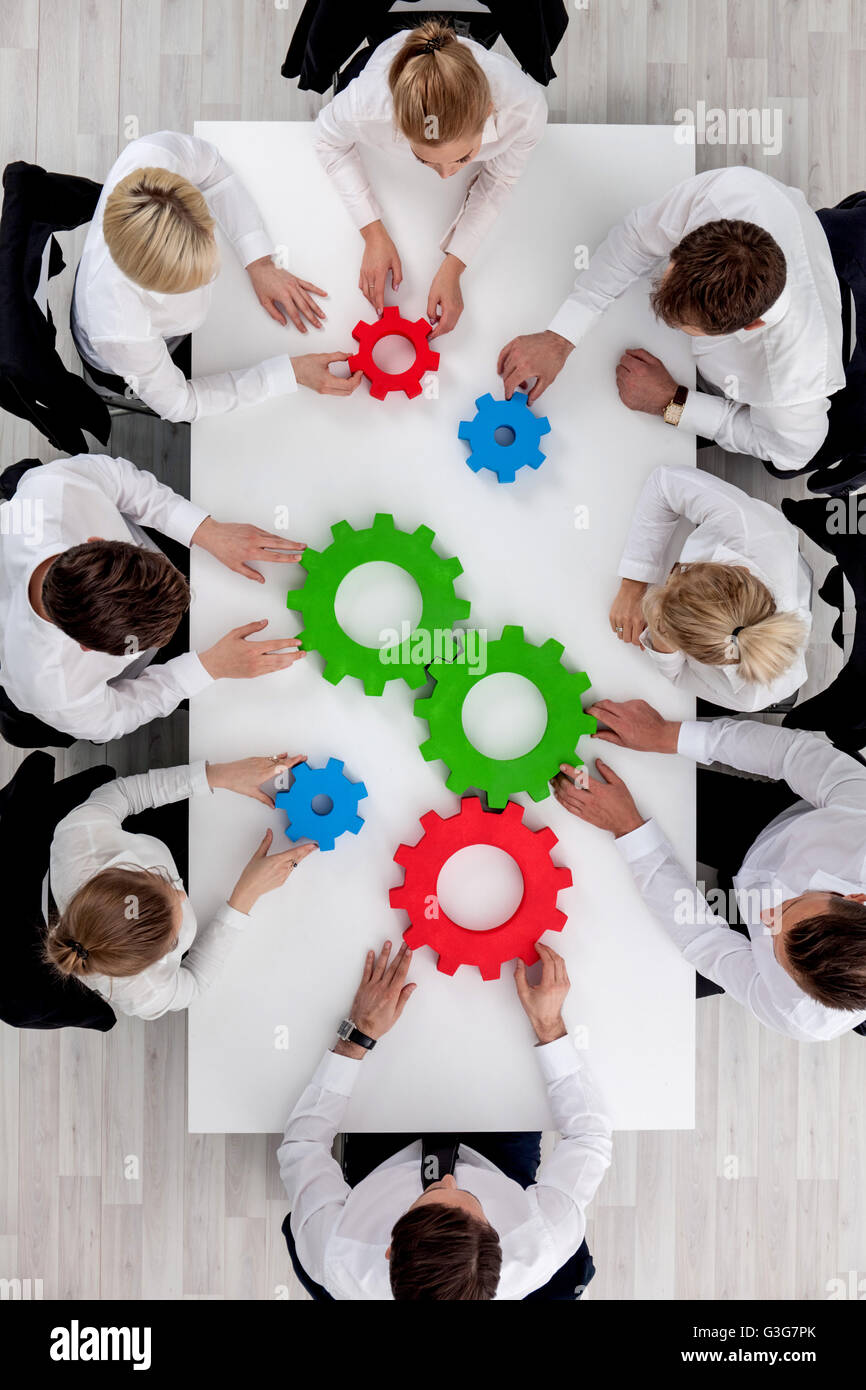 Business team sitting around the table with cogs, teamwork concept ...