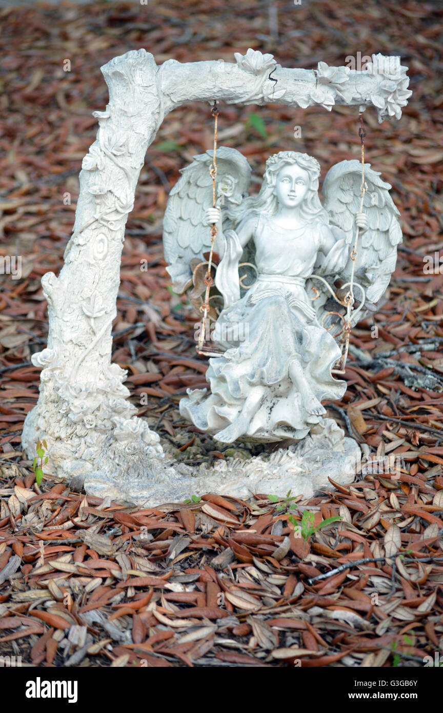 A white, stone, ornate, decorative angel on a wire swing with leaves ...