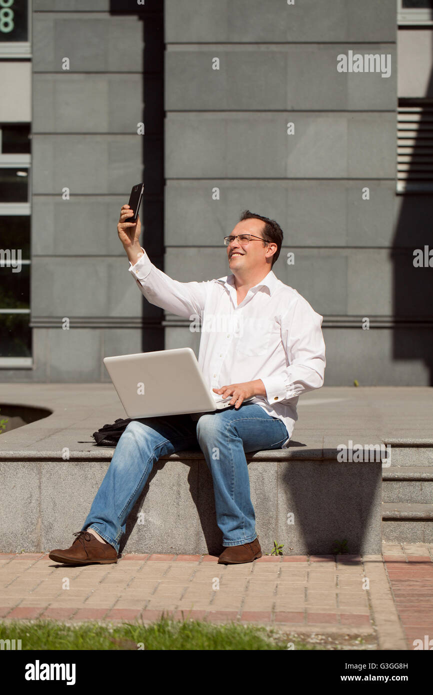 Adult caucasian businessman with computer sitting outdoors sunny day ...