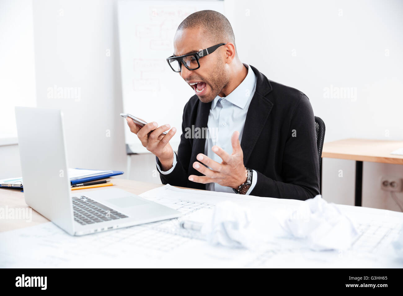 Angry businessman in stress working and talking on mobile phone at ...