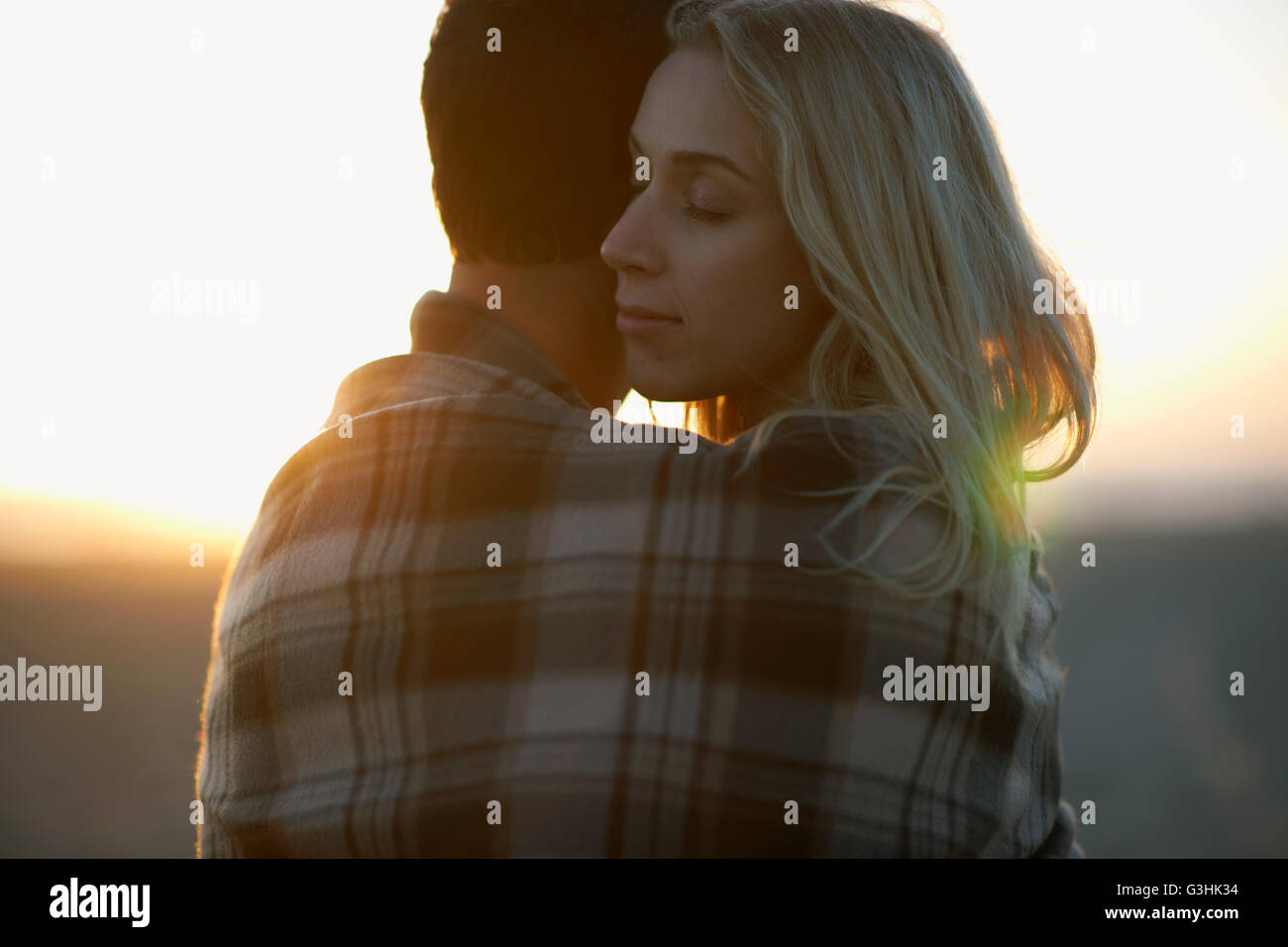 Couple hugging outdoors, at sunset, wrapped in blanket Stock Photo - Alamy