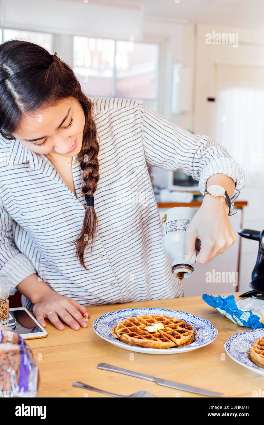 Woman in kitchen pouring maple syrup on fresh waffle Stock Photo - Alamy