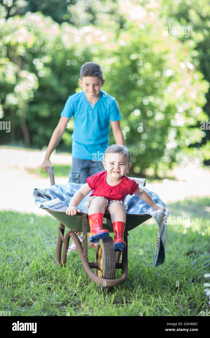 Young boy pushing sister in wheelbarrow Stock Photo - Alamy